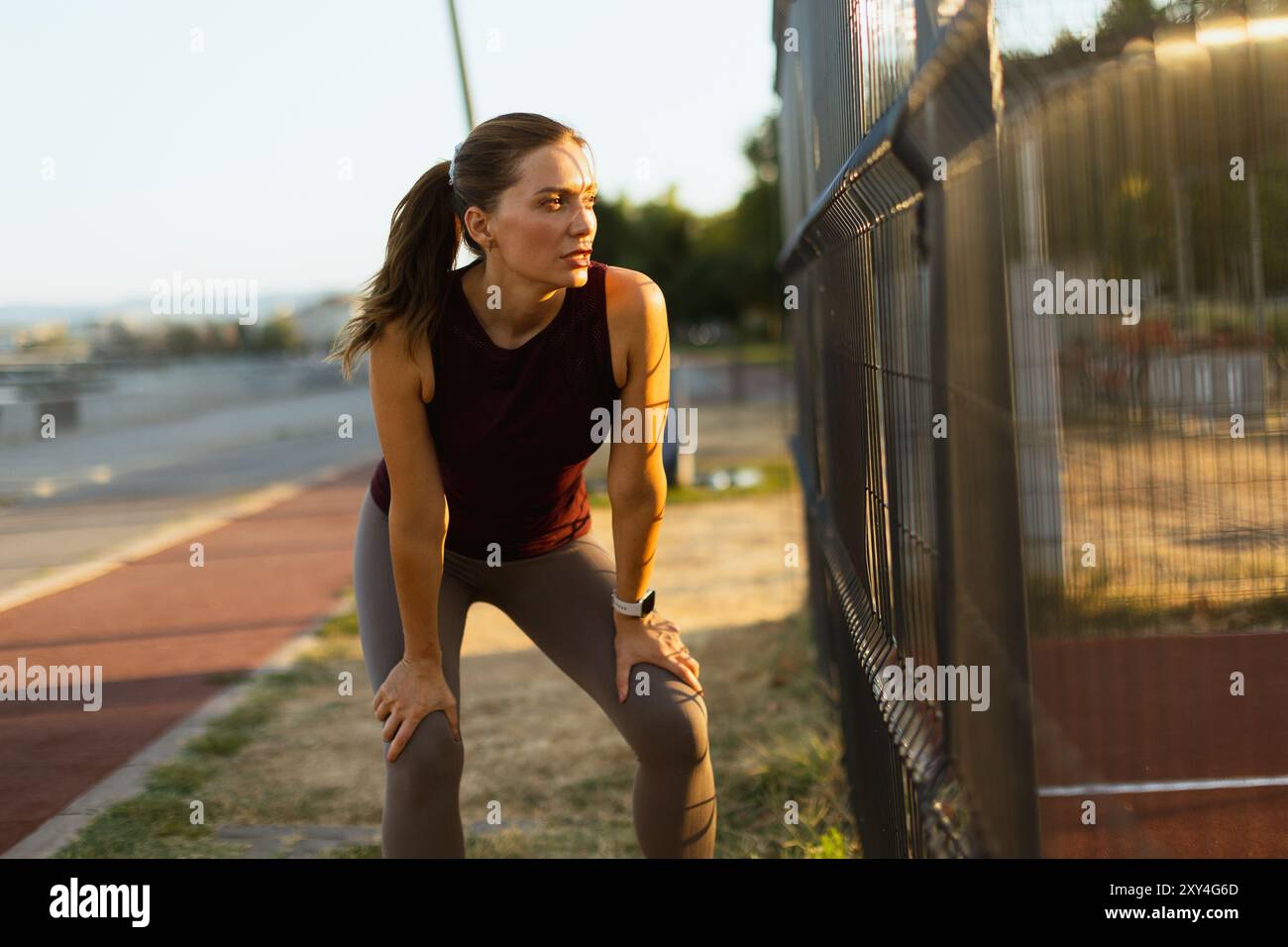 In the golden glow of sunset, a focused woman leans against a fence ...