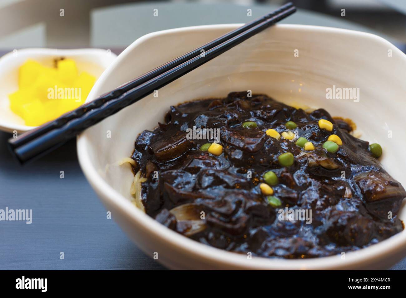A pair of chopsticks rests on top of a bowl of jjajangmyeon, a ...