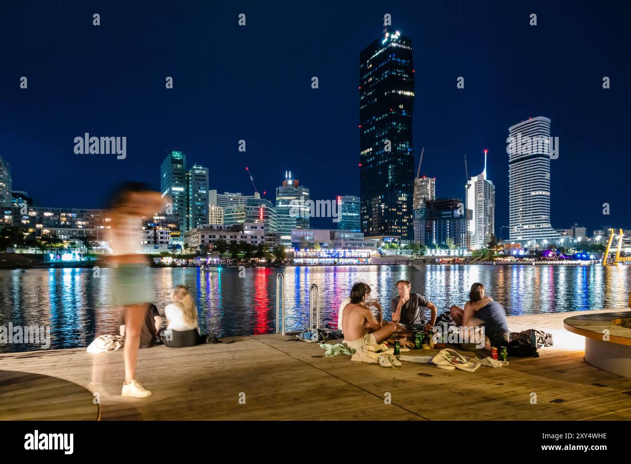 Young people sitting on a wooden deck on the bank of the New Danube in ...