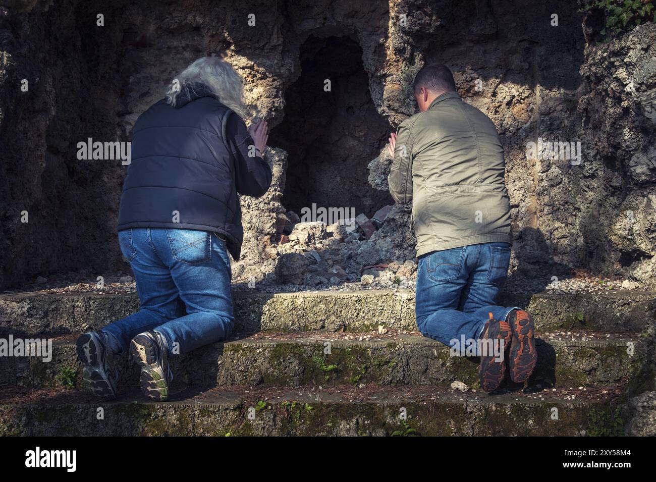 Two men kneeling in prayer on the steps in front of a grotto Stock ...