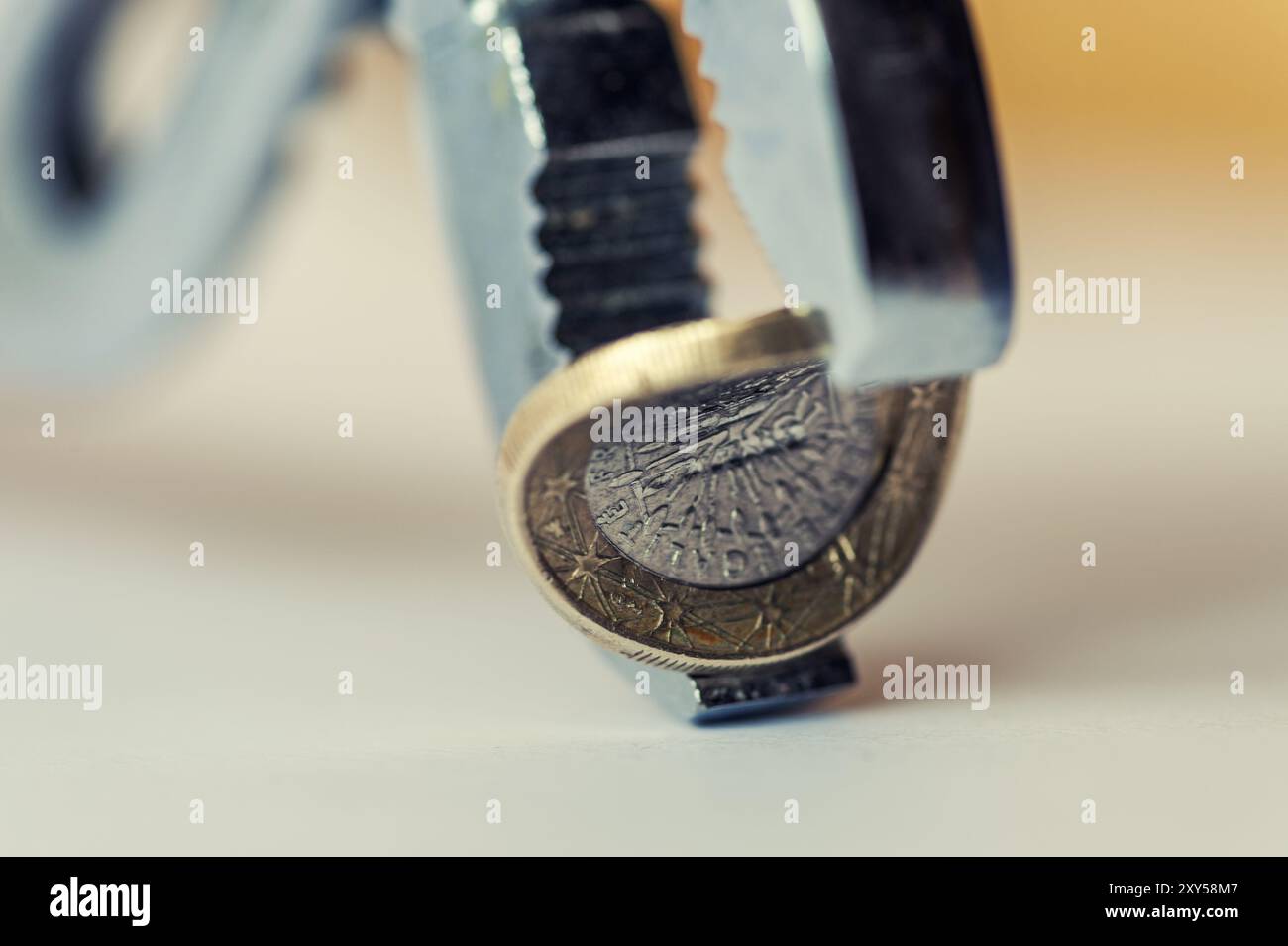 A bent euro between the jaws of a pair of pliers with a concave bend ...