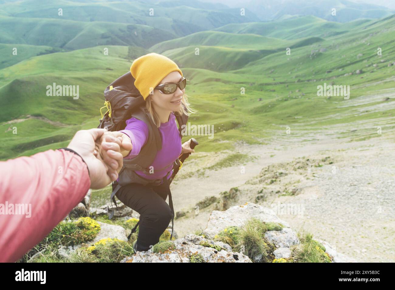 A climber helps a young mountaineer woman reach the top of the mountain ...