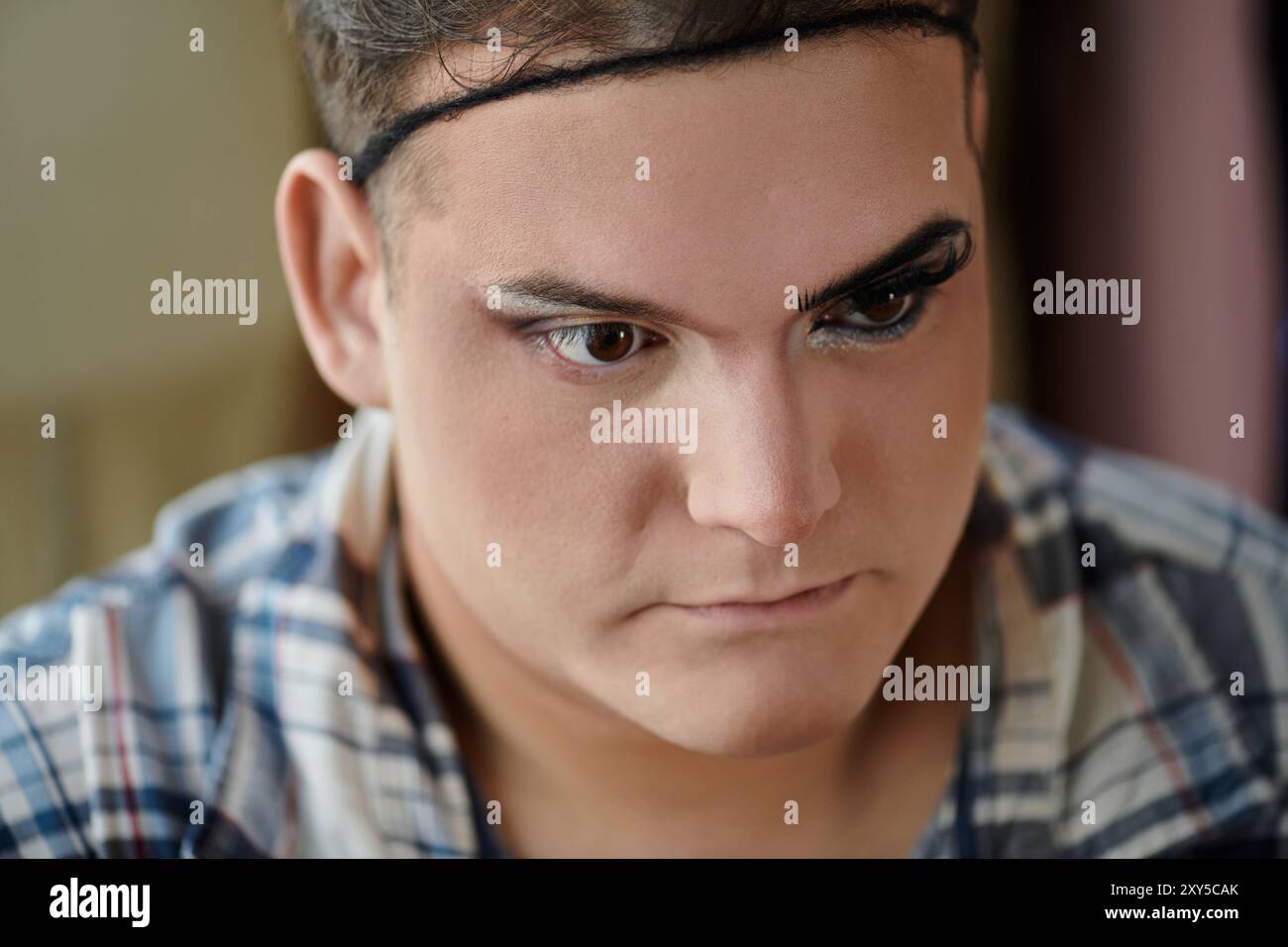 A queer person with bold makeup looks down, their expression unreadable ...