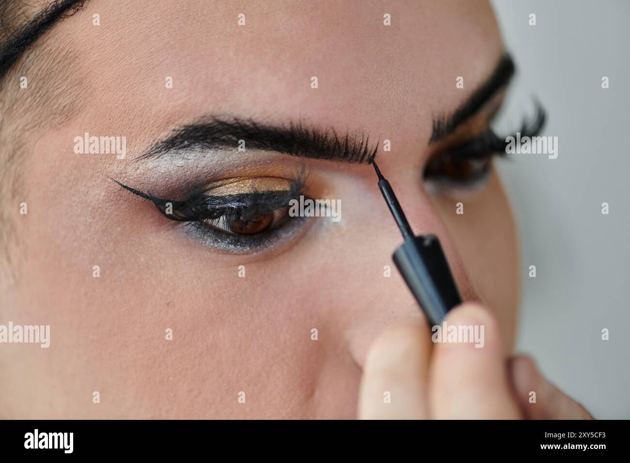 A queer person applies eyeliner to their upper eyelid Stock Photo - Alamy