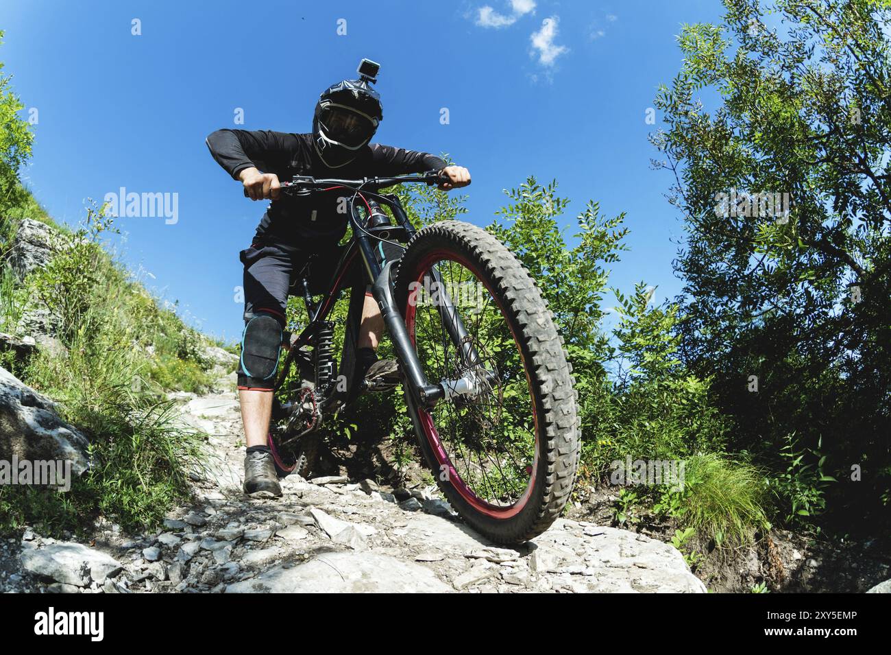 A young rider on a bicycle for downhill descends the rocks in the ...