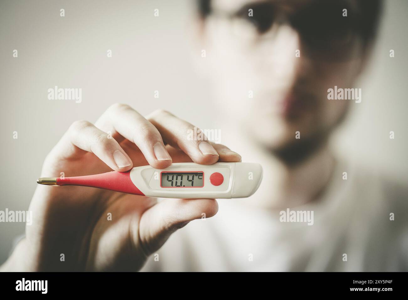 Man holds a red fever thermometer with high temperature in his hand ...