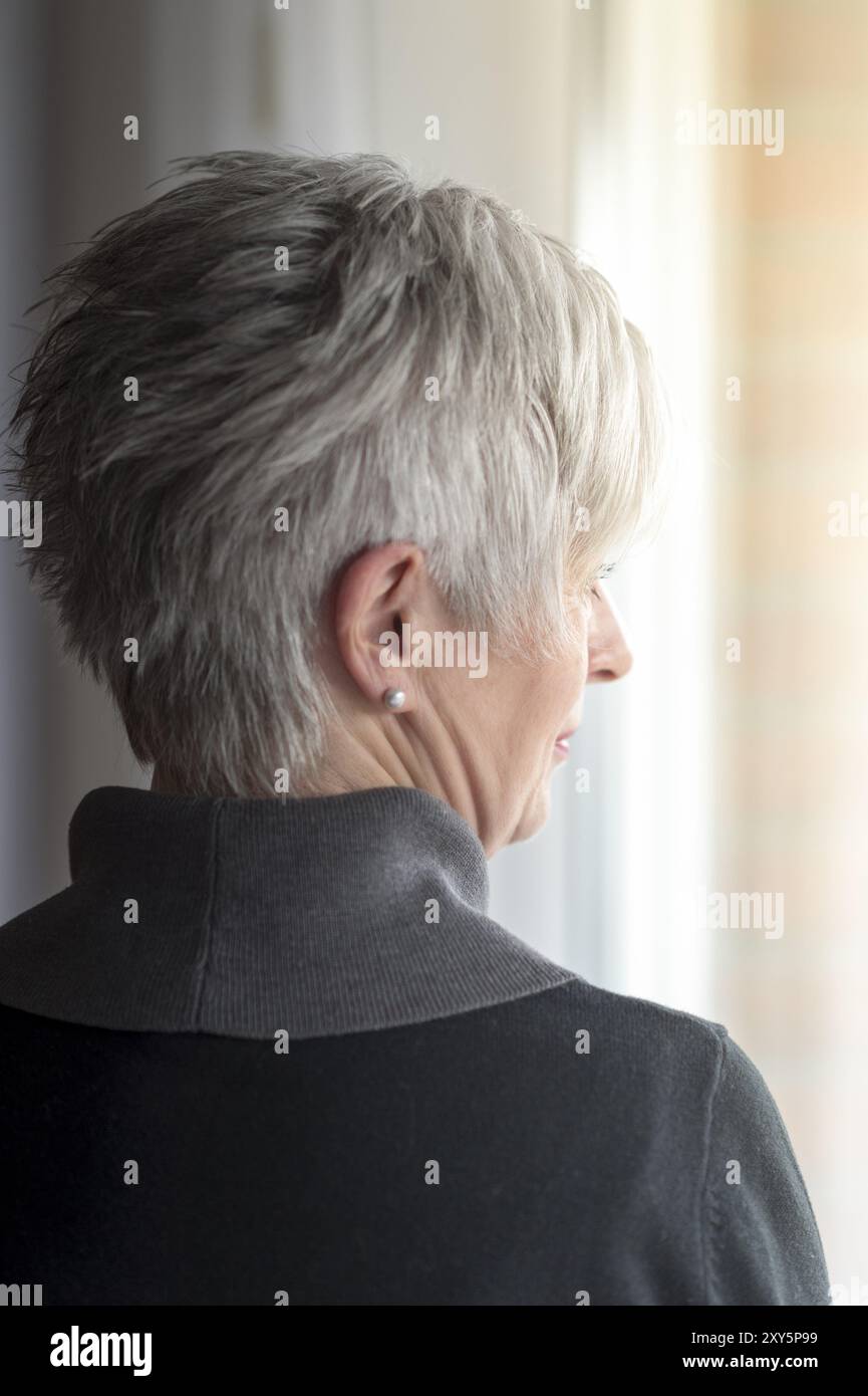 Rear view of an elderly lady with grey hair looking thoughtfully out of ...
