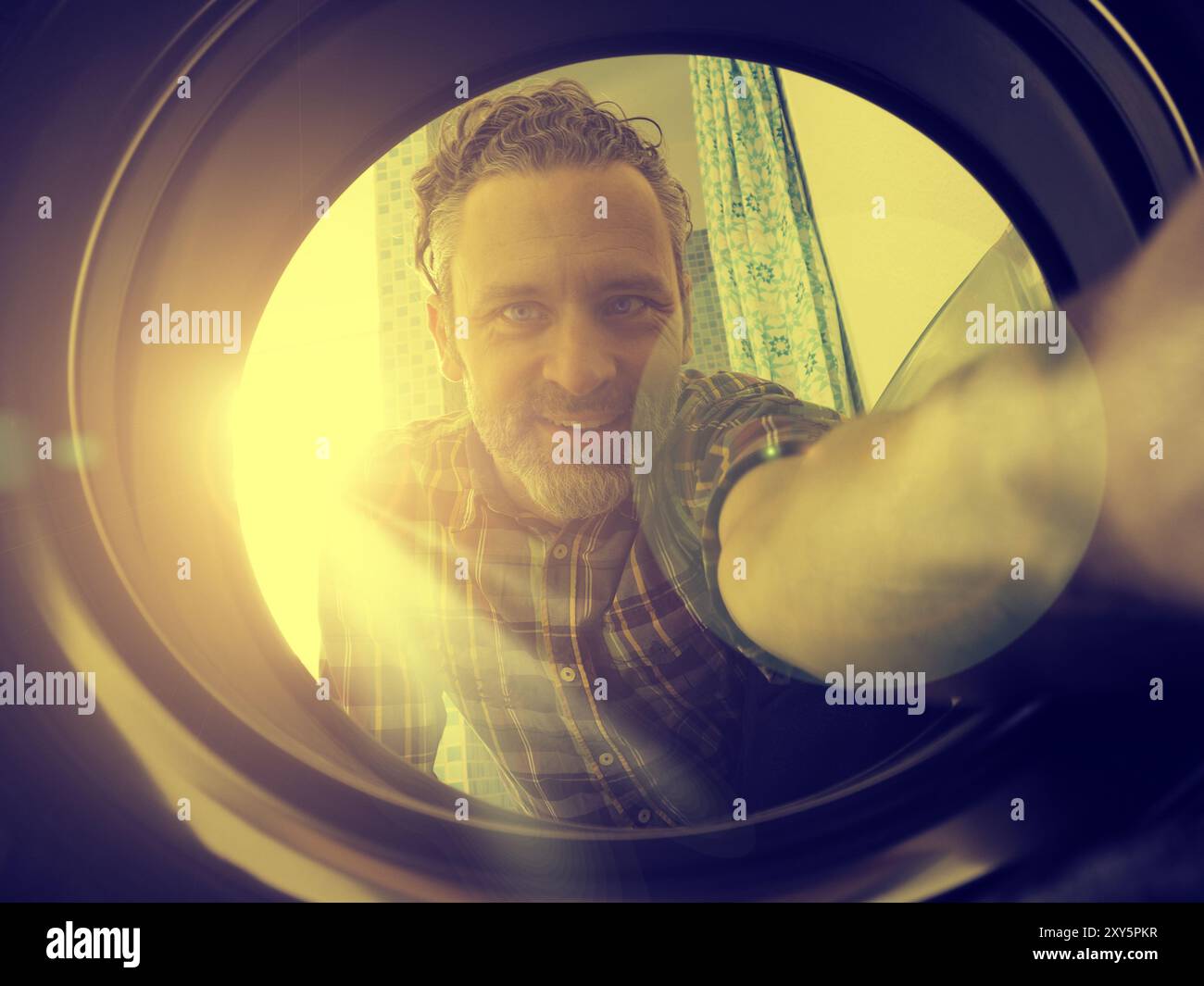 Happy man loading the washing machine, bright sun in the back, golden ...