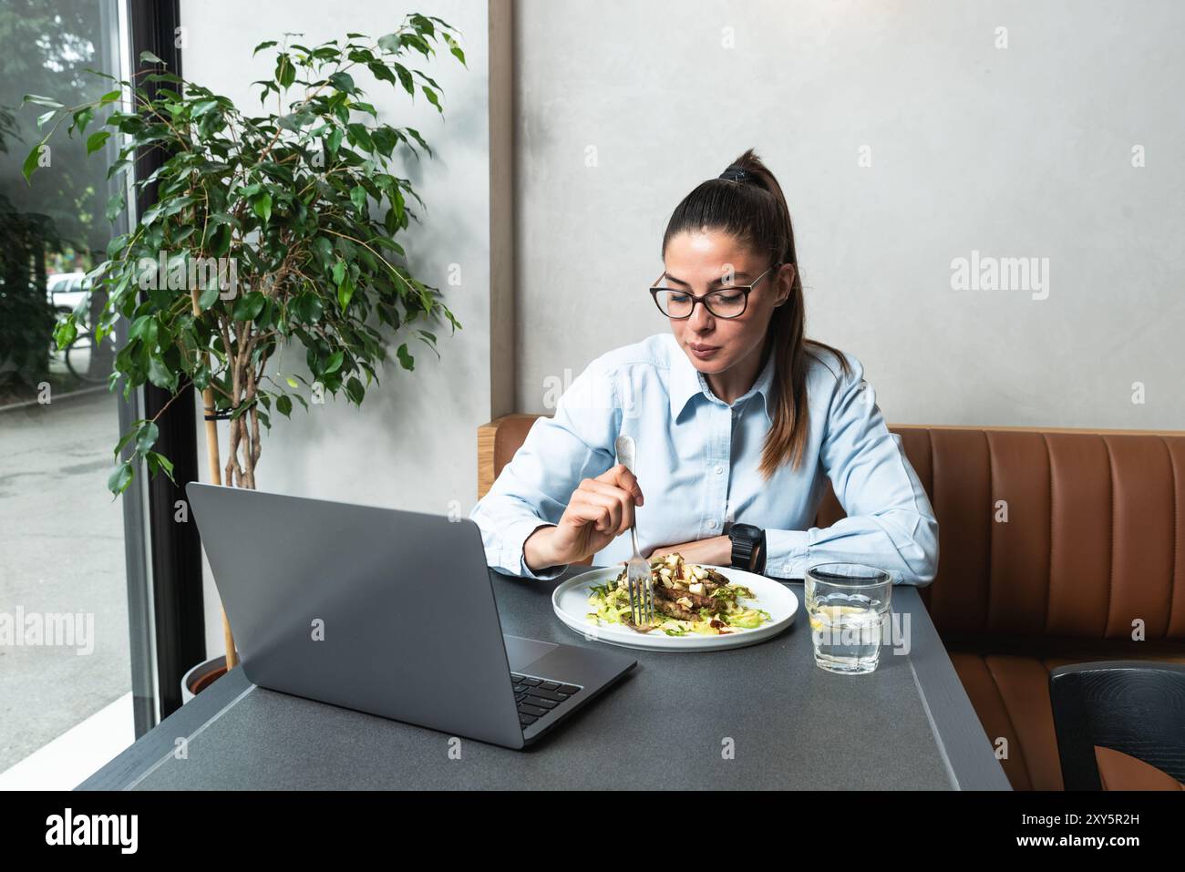 Young business woman working remotely from cafeteria during lunch break ...