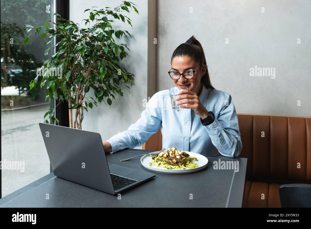 Young business woman working remotely from cafeteria during lunch break ...
