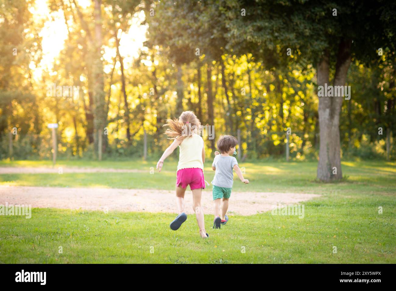 Two kids, back view, siblings, running on the grass at the park at ...