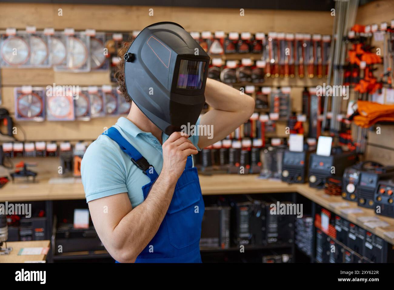 Workman in overalls choosing protective plastic welding mask at ...