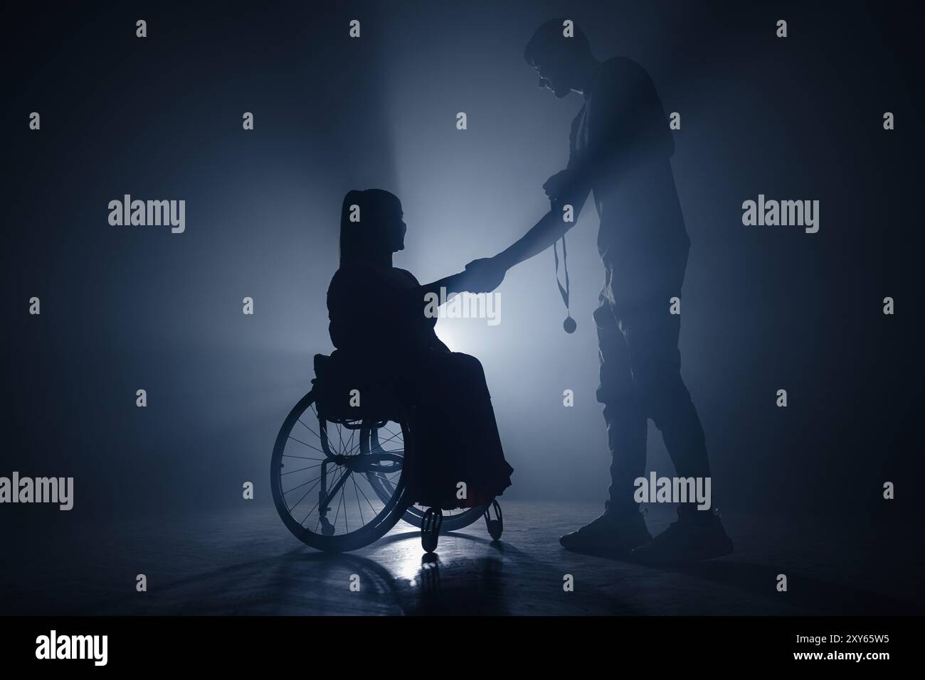 Woman in a wheelchair receiving a medal from a man on a dark stage ...