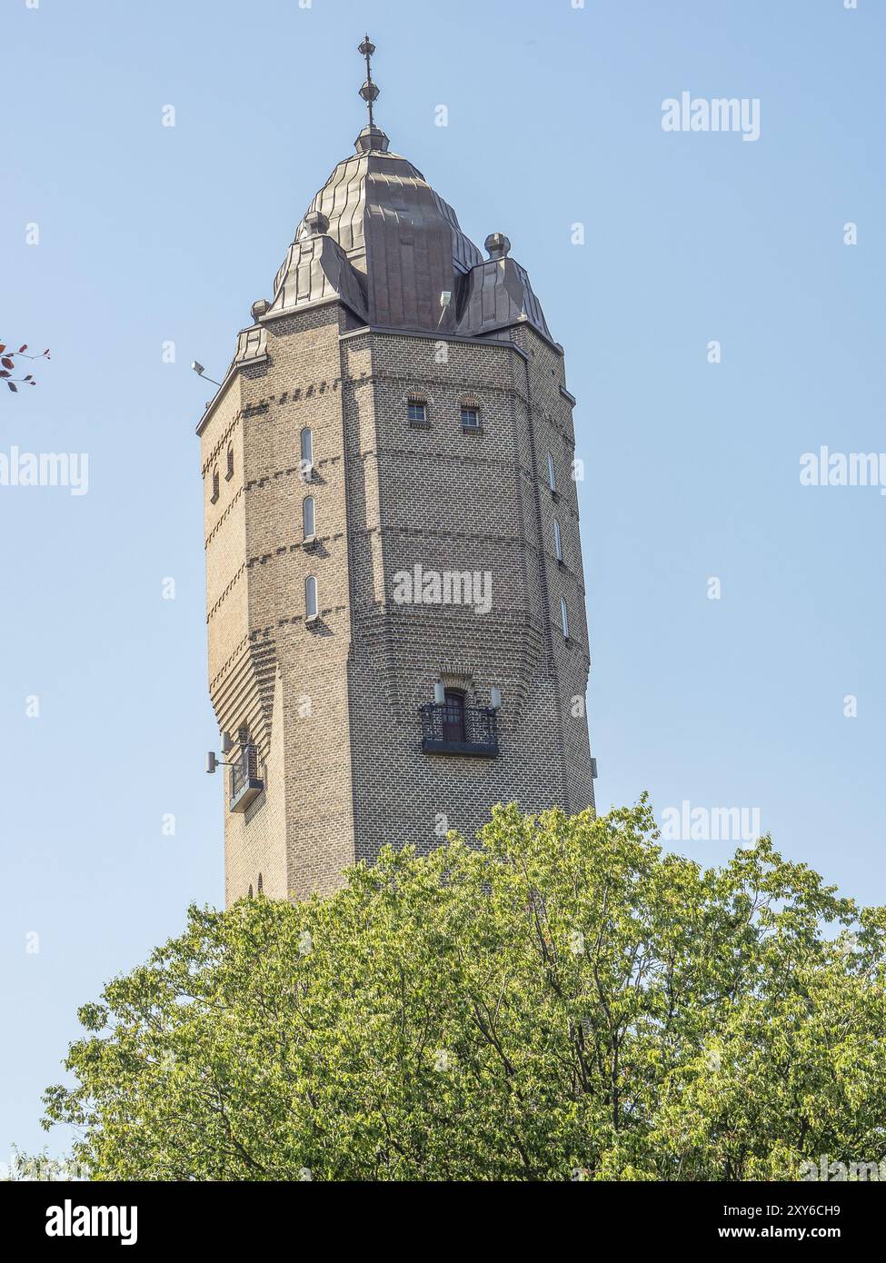 A historic tower rises above green trees in a sunny blue sky ...