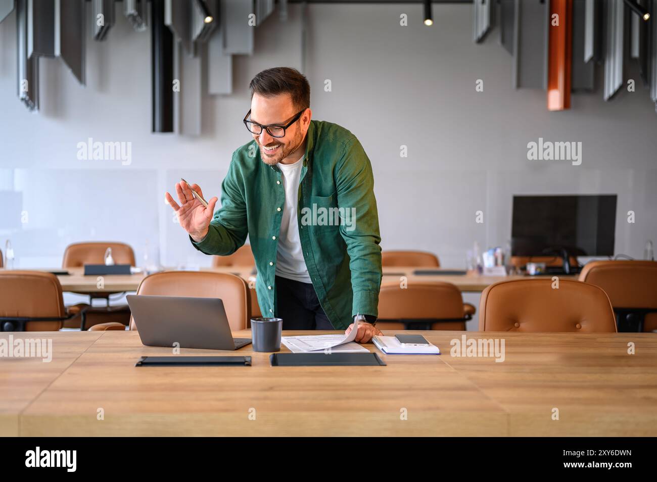 Male accountant smiling and waving hand to client over laptop on desk ...