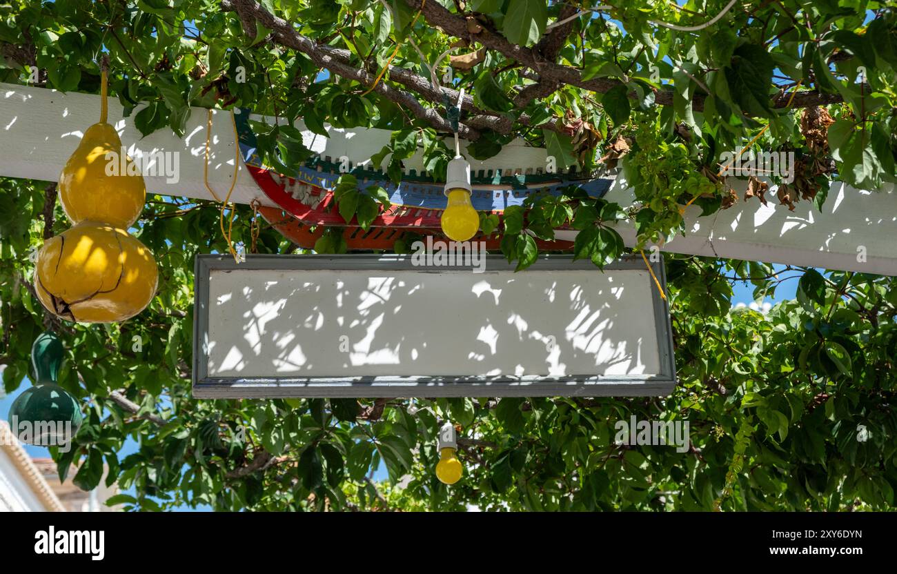 Empty wooden sign hanging from a vine arbor, traditional greek island ...