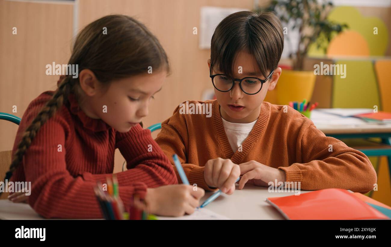 Two Caucasian pupils classmates in school lesson class together write ...