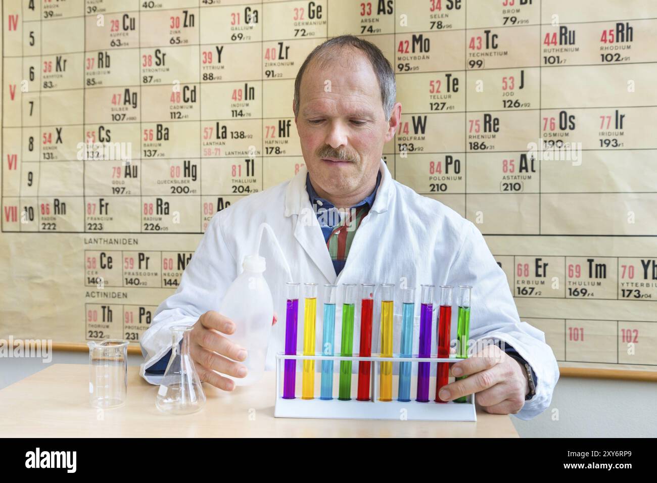 Chemist in lab coat filling colorful test tubes near periodic table ...
