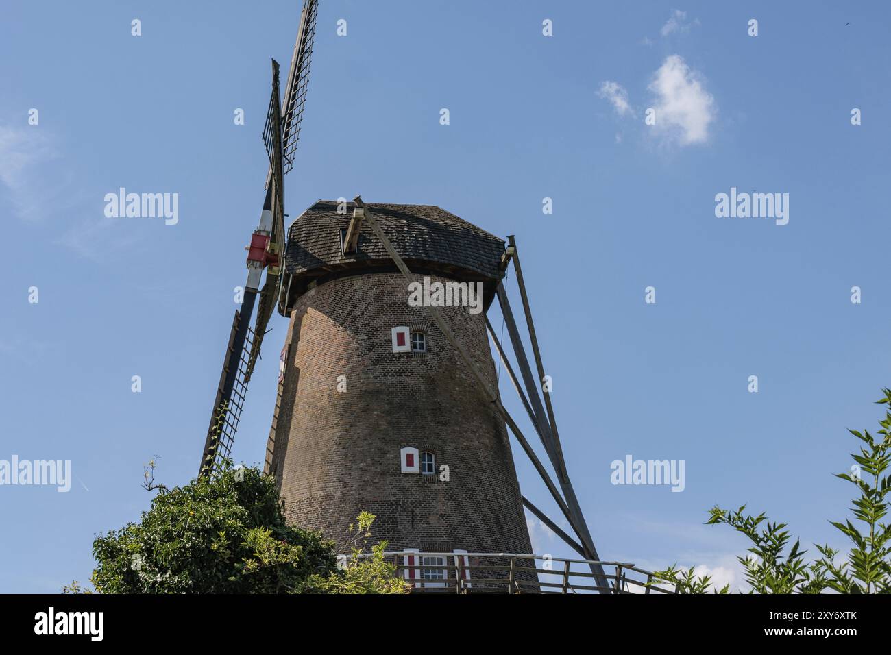 Historic windmill with wooden sails and brick building under a bright ...