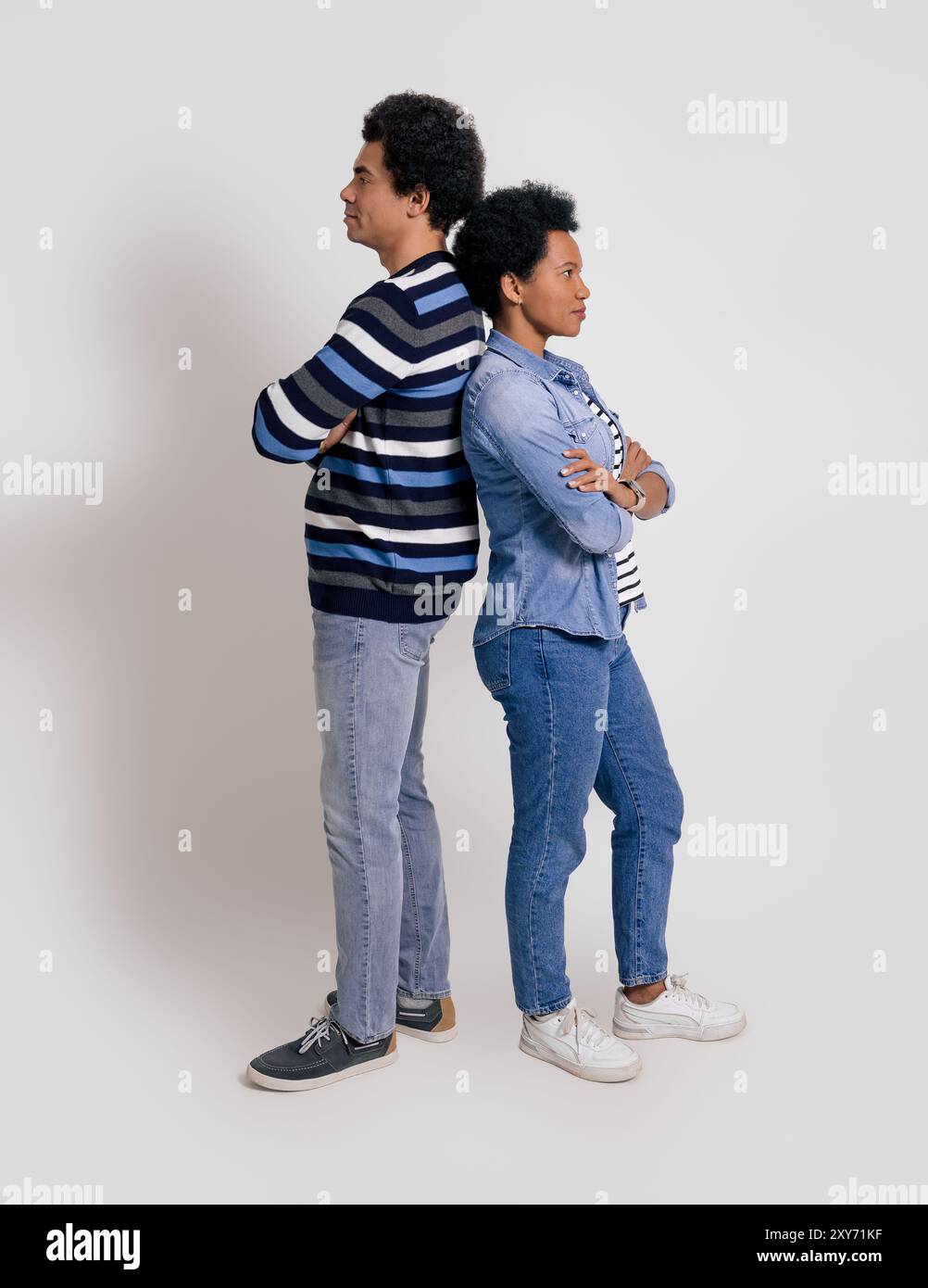 Side view of young couple with arms crossed standing back to back and ...