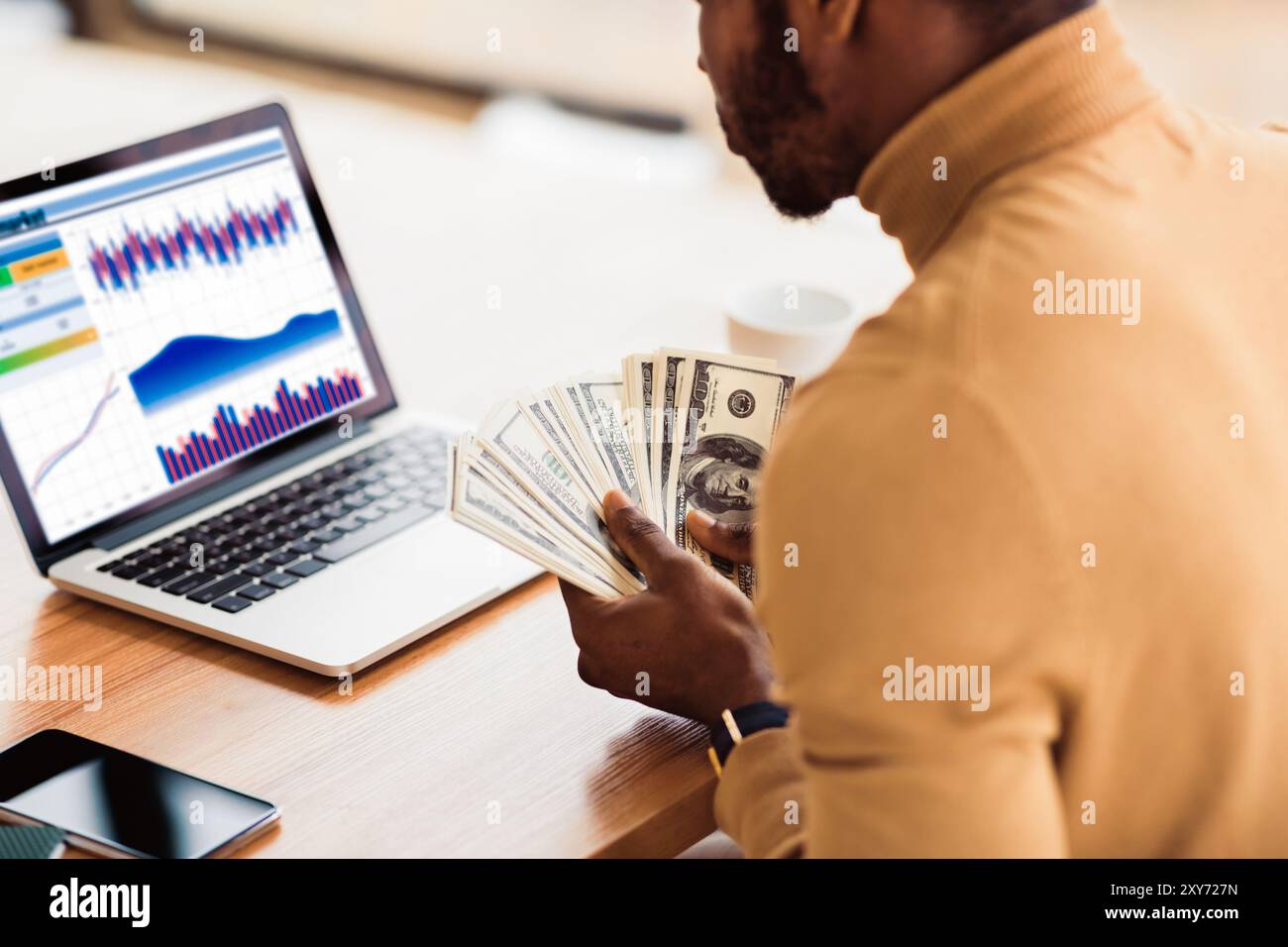 Black manager working with diagrams on pc holding dollars Stock Photo ...