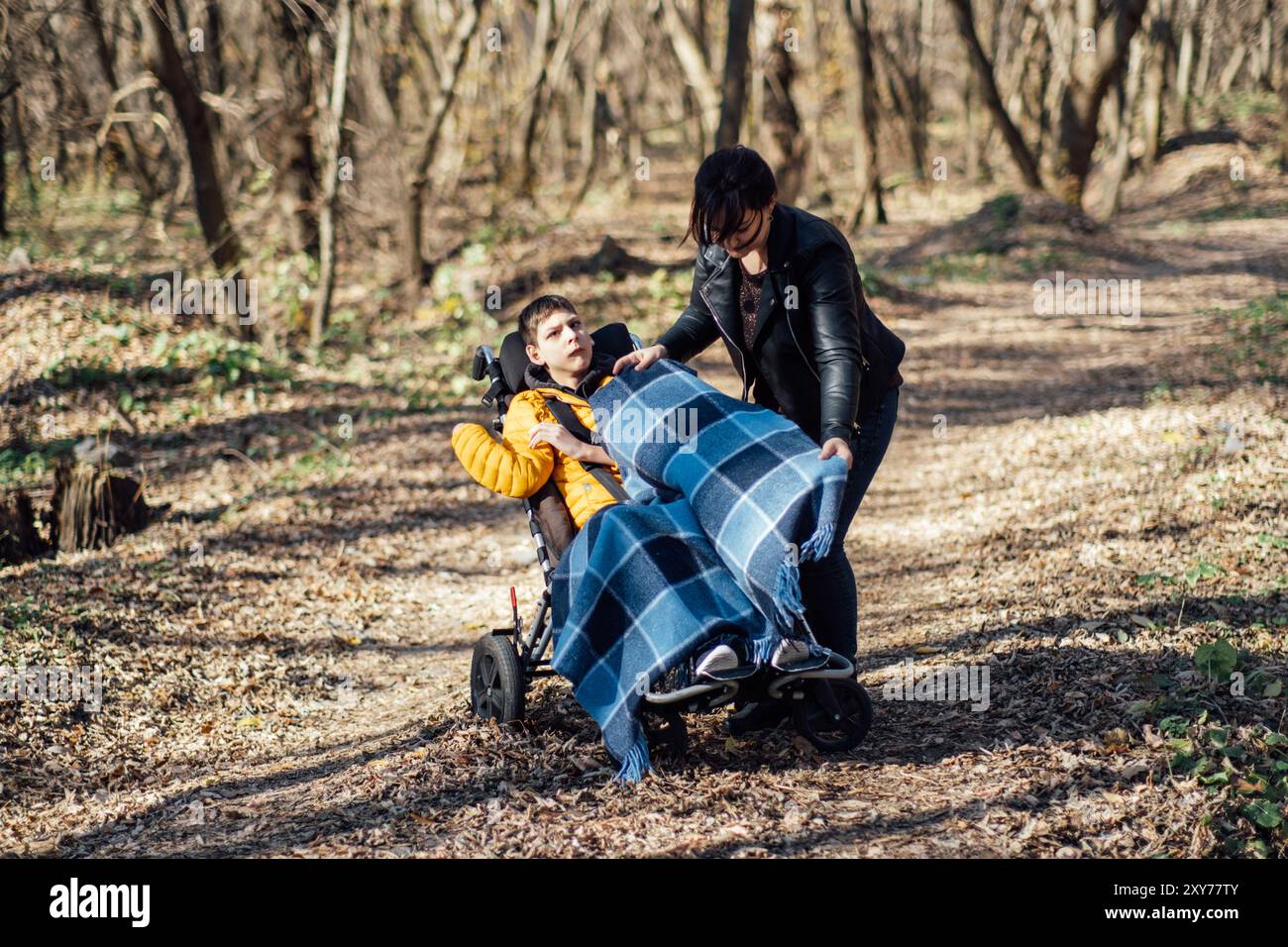 Mother adjusting blanket for child in wheelchair during outdoor walk in ...