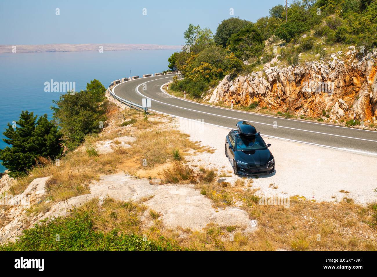 Black car with a roof box, parked at the edge of a narrow, winding road ...