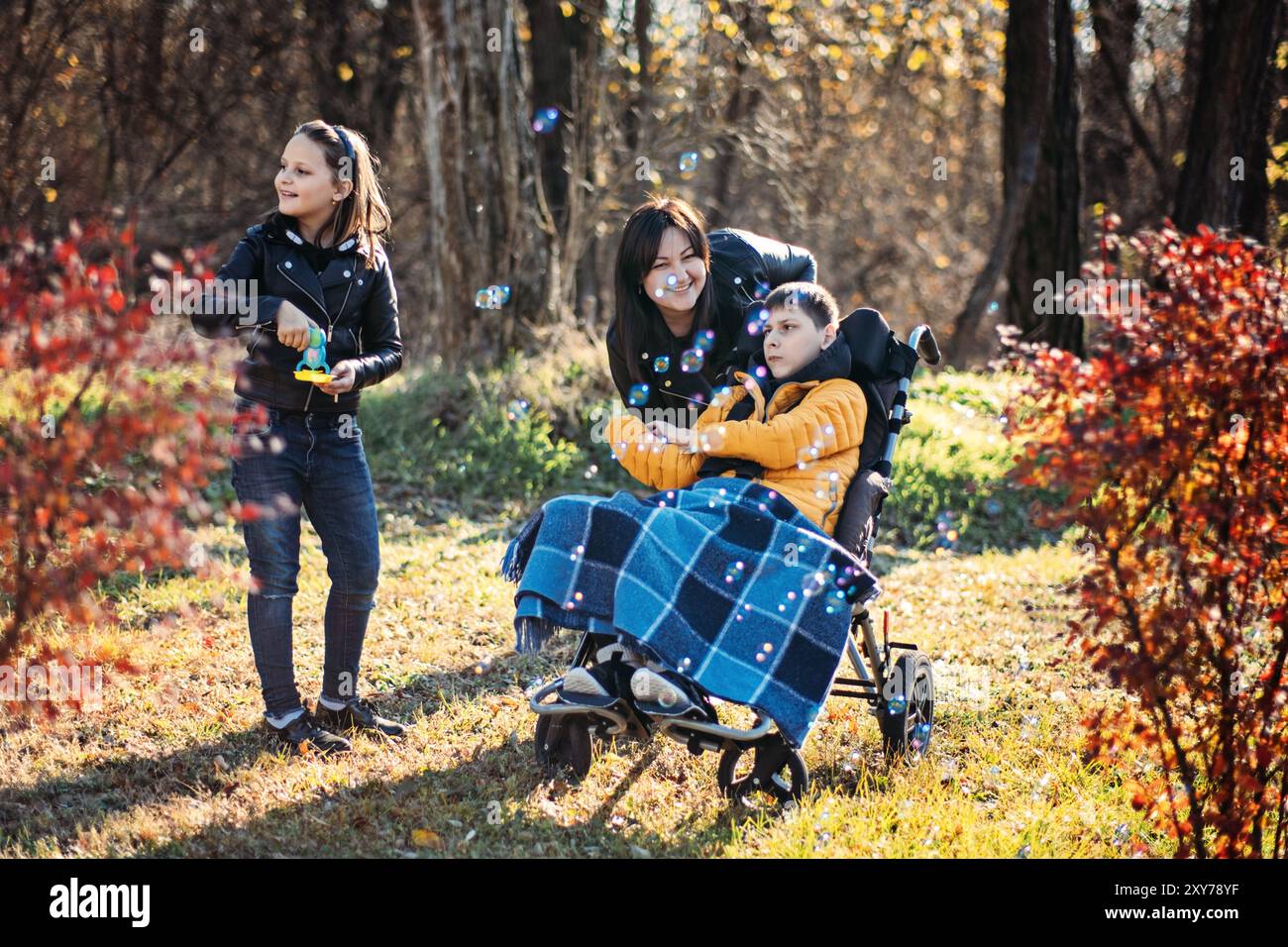 Mother and sibling playing with bubbles with child in wheelchair ...