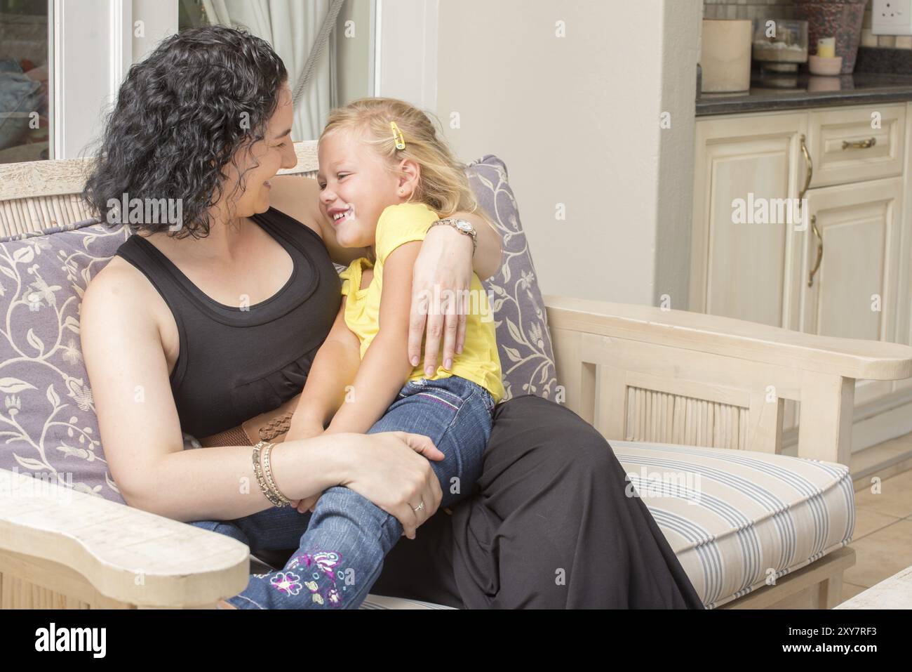 Daughter sitting on mother's lap outside on the porch of their house ...