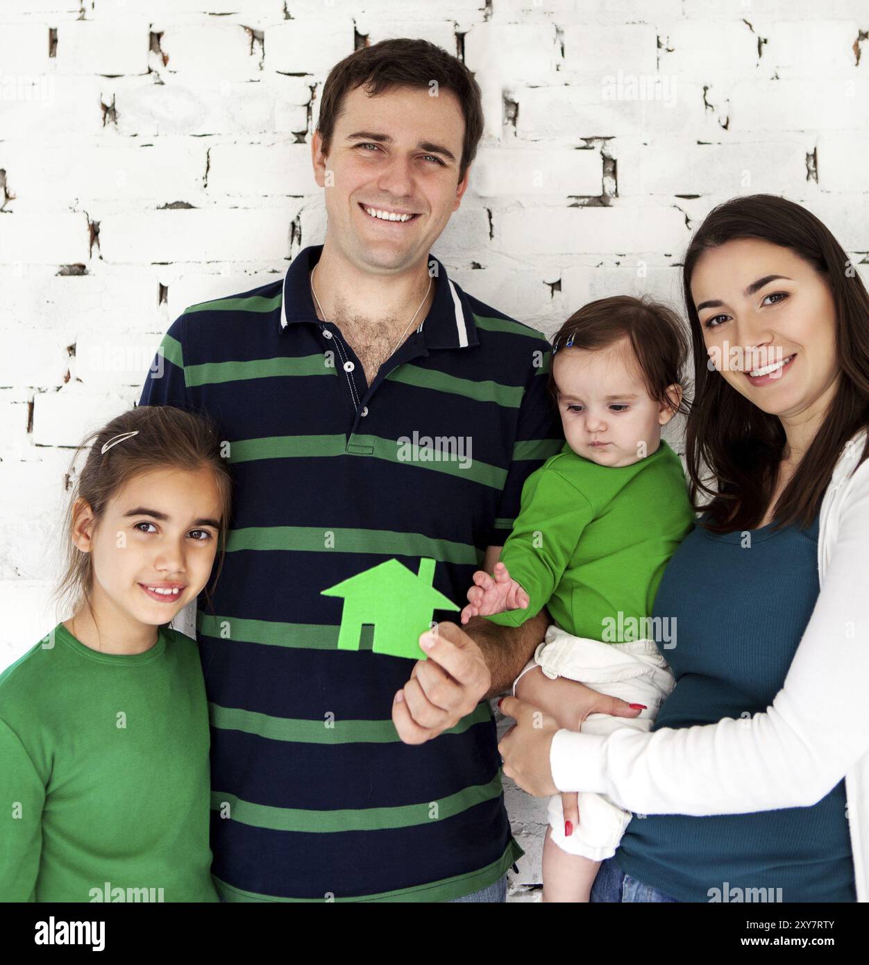 Portrait of a happy smiling family with little green house near white ...