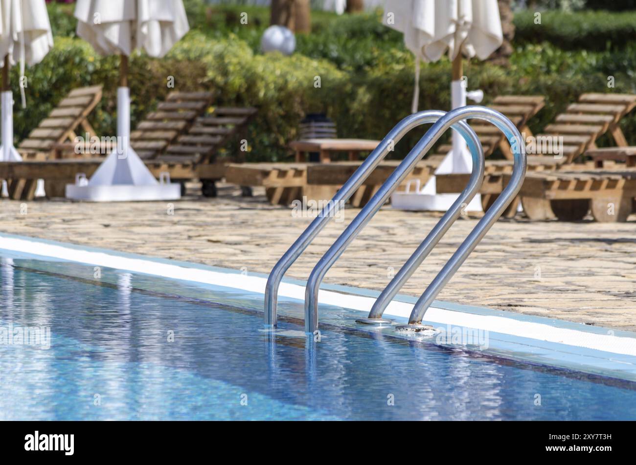 Handrails by the pool with blue water on the background of sun loungers ...