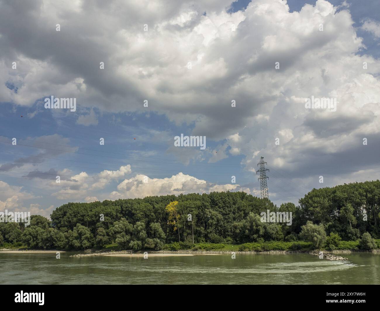 River landscape with dense forest, high power pole and changing sky ...