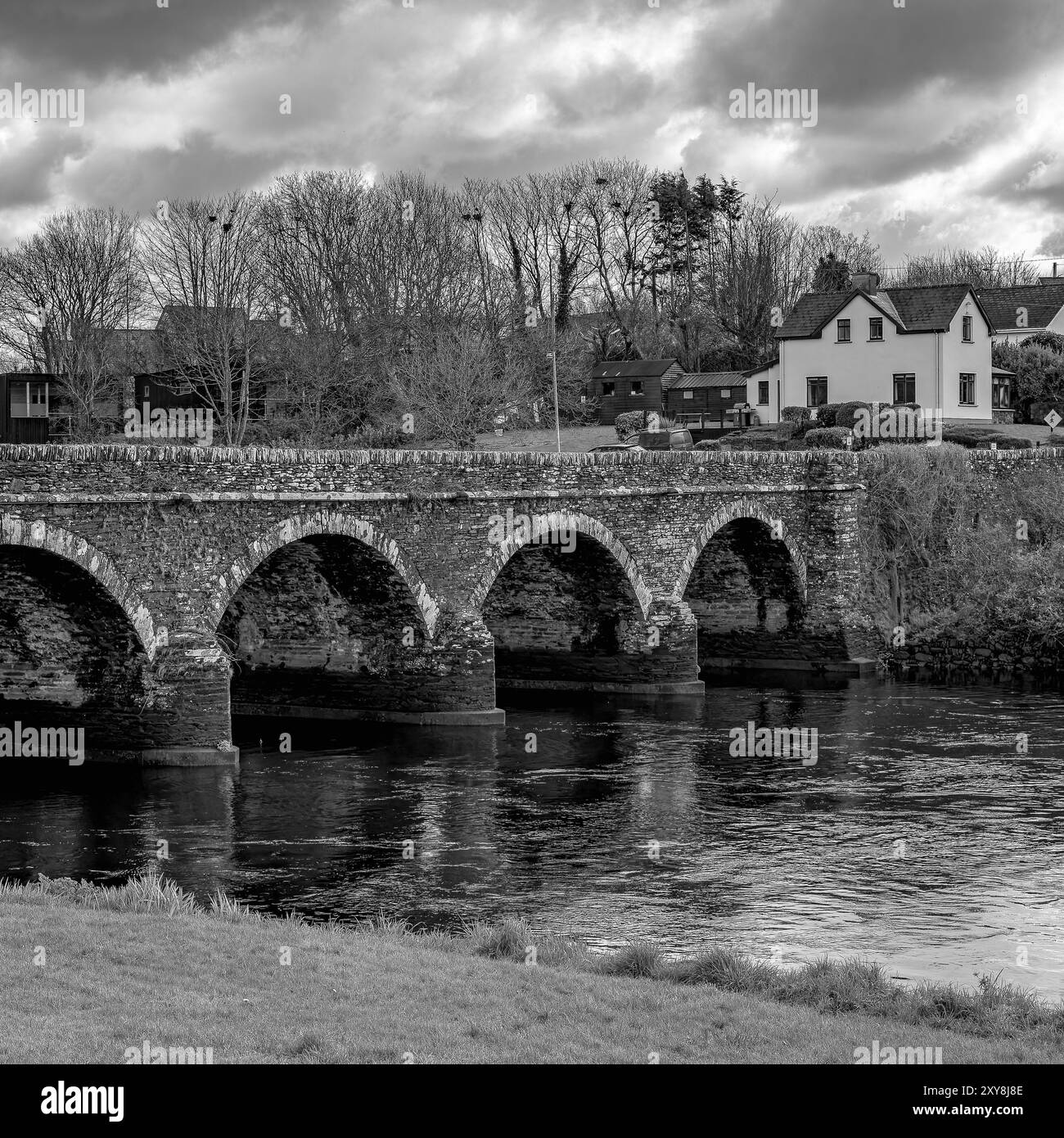 A stone bridge with arches spans a river, leading to a small village ...