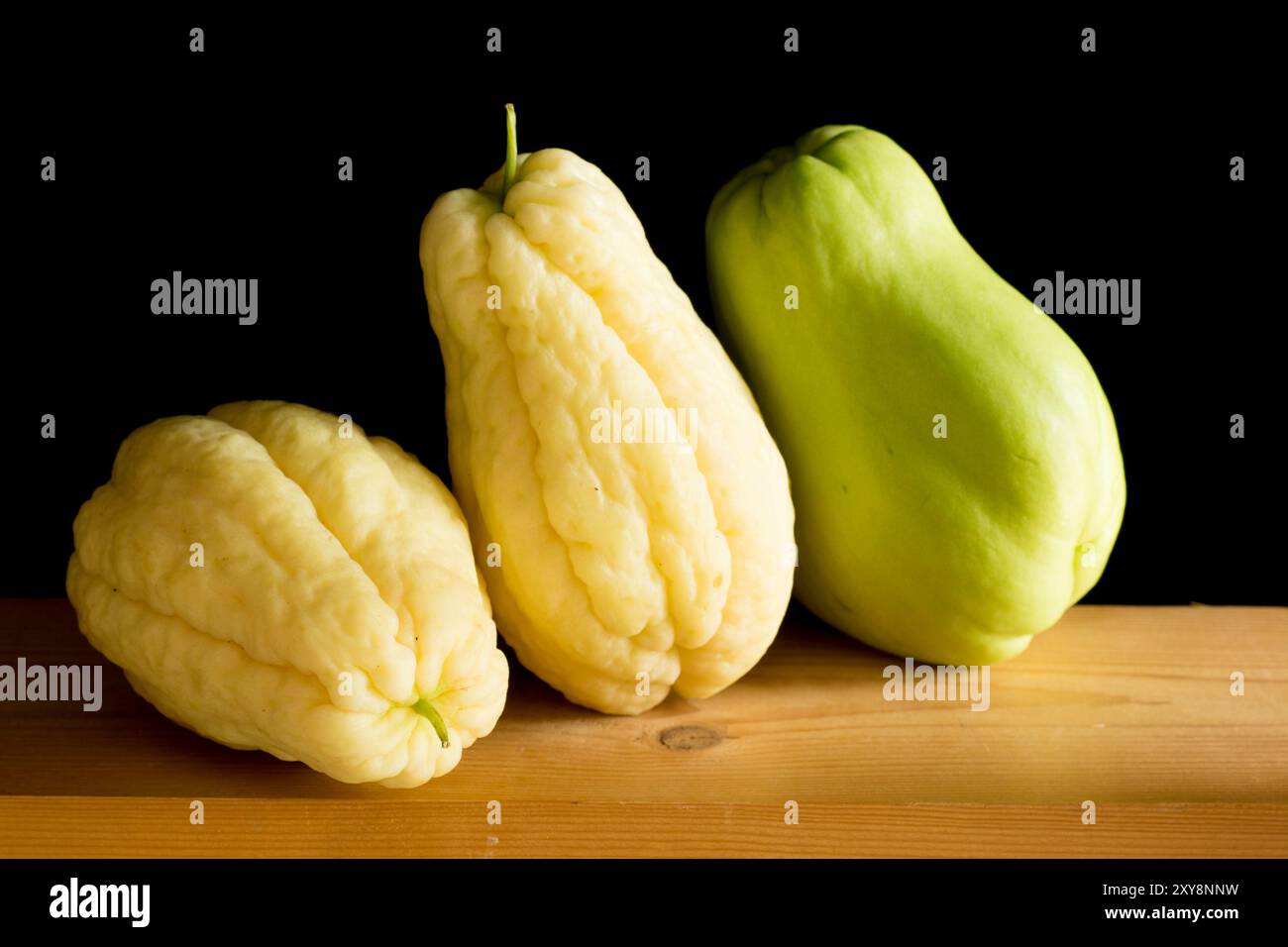 Three beautiful Chayotes on a wooden shelf against a black background ...