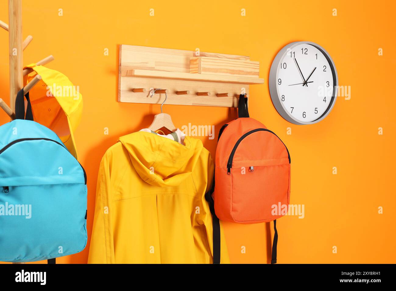 Bright backpacks, cap, coat and clock near orange wall Stock Photo - Alamy