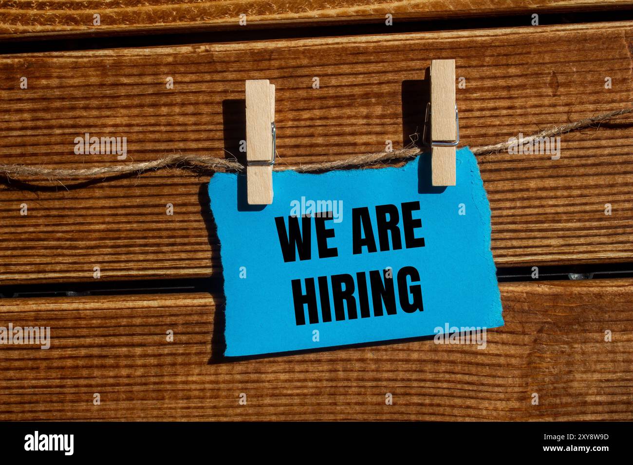 We are hiring message written on ripped torn blue paper piece with wooden background. Conceptual ...