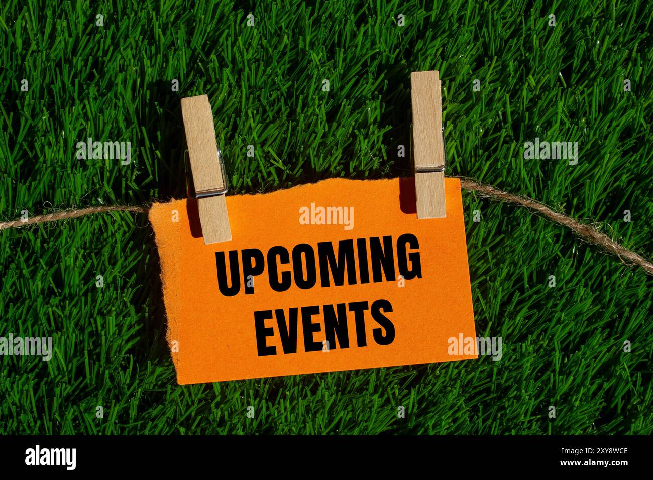 Upcoming events words written on ripped torn orange paper piece with green grass background ...