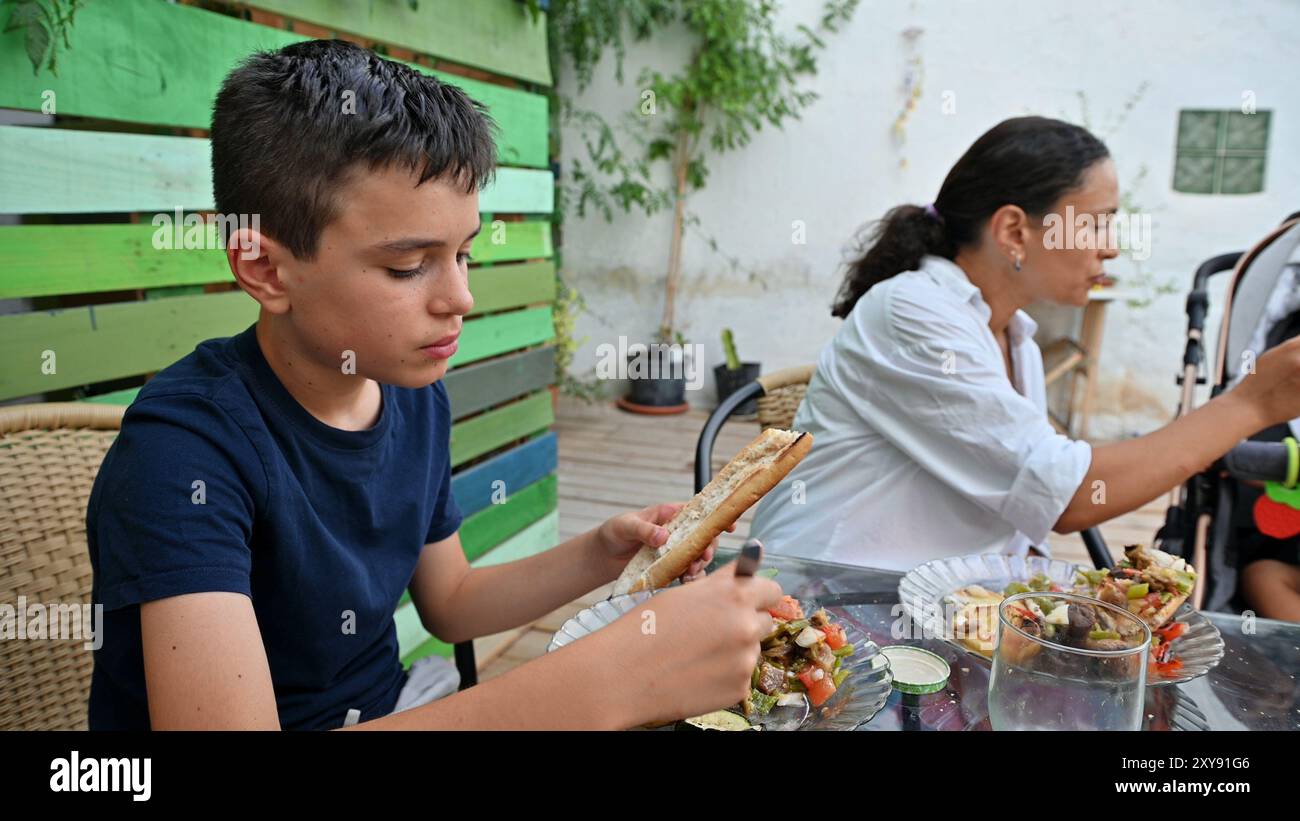 A family enjoys a relaxed meal outdoors, featuring various dishes in a ...