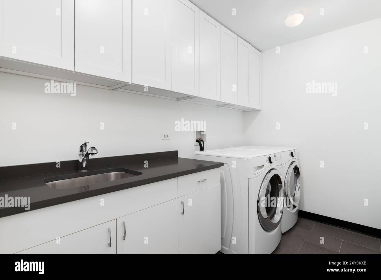 A laundry room with white cabinets, black quartz countrop with a sink ...
