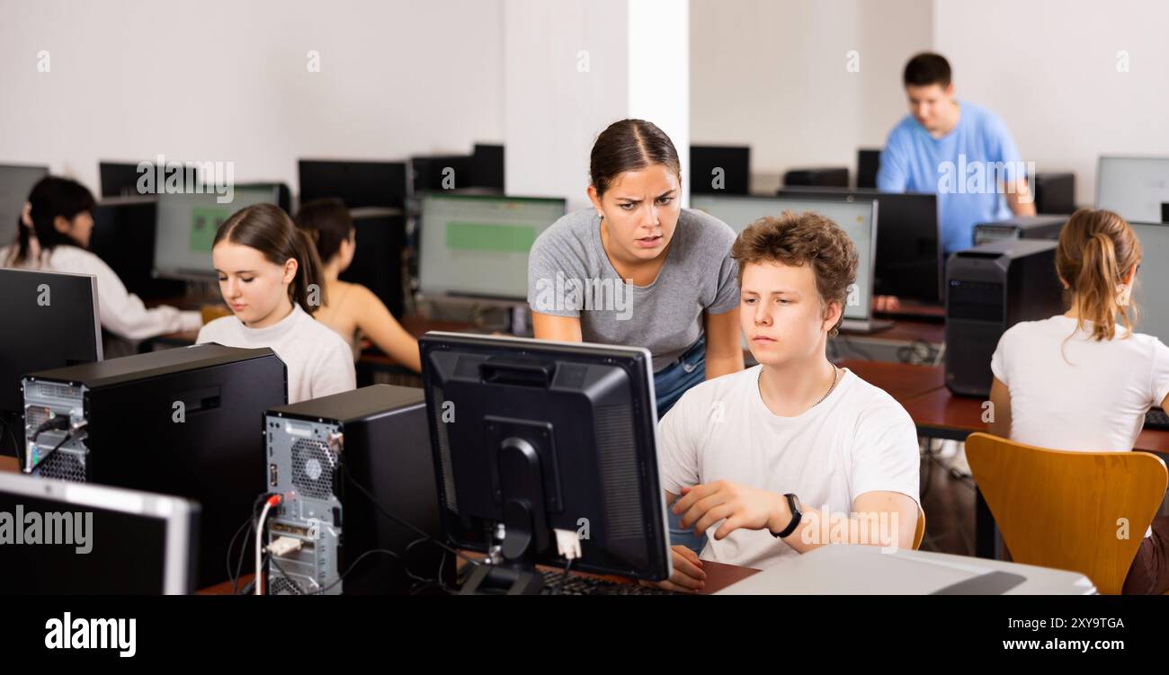 Schoolboy using computer and teacher helping to him in class room Stock ...