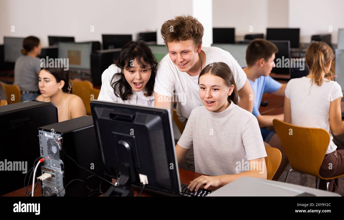 Portrait of multinational young students group emotionally reacting while studying at pc in ...