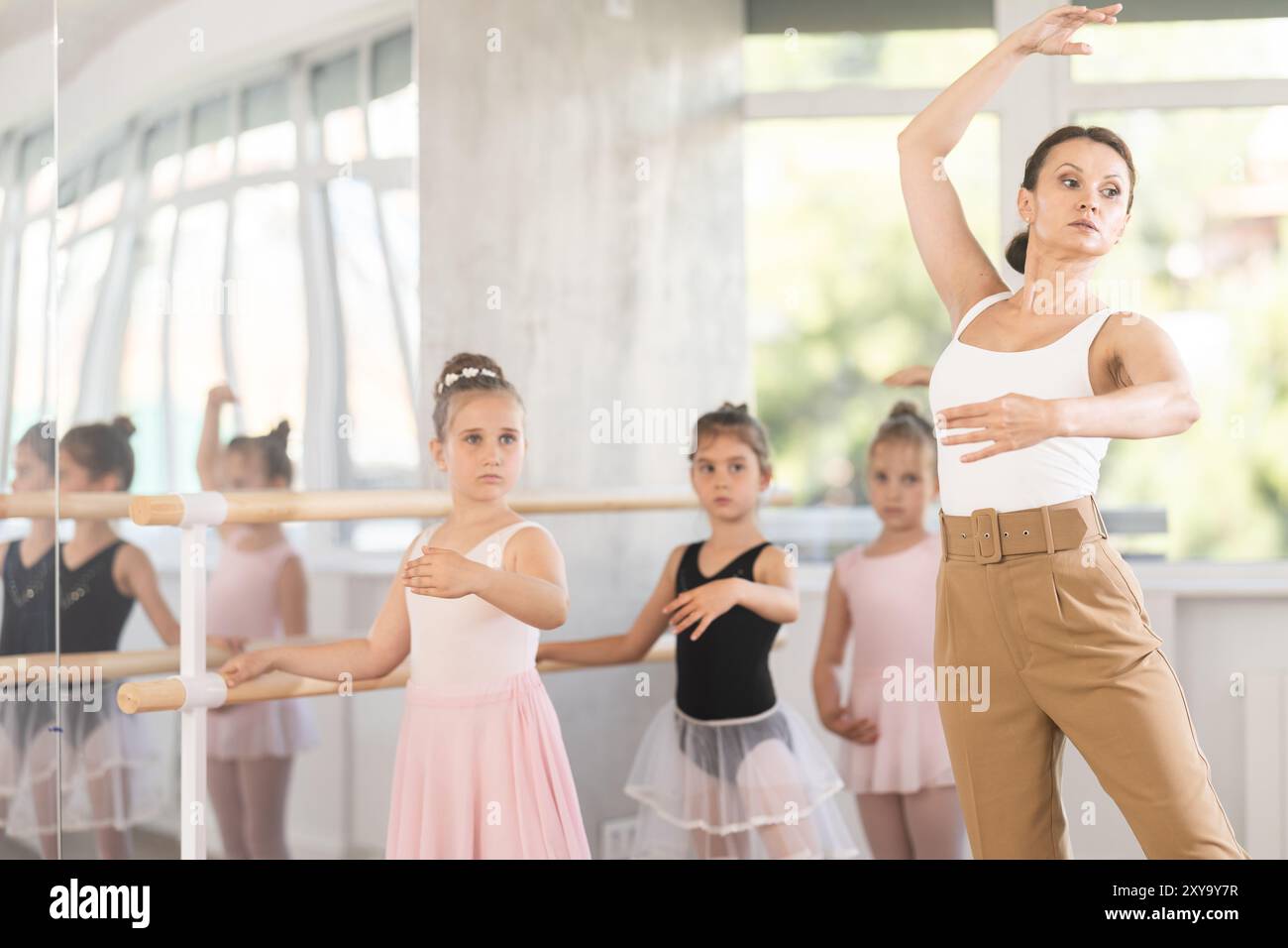 Girl students of choreographic school look at woman teacher and repeat ...