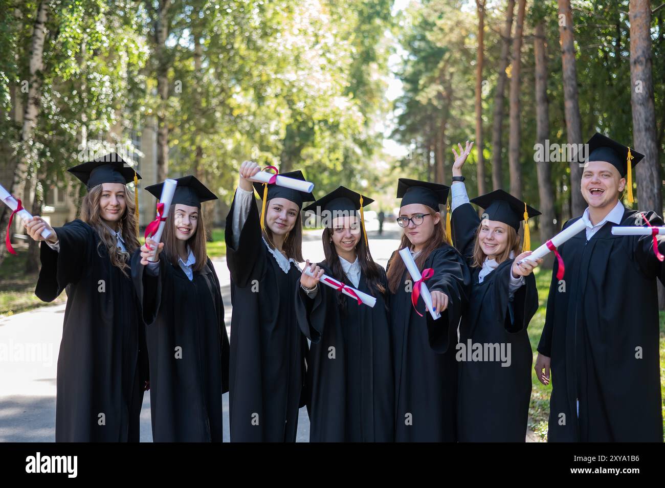 Row of young students in graduation gowns outdoors showing off their ...