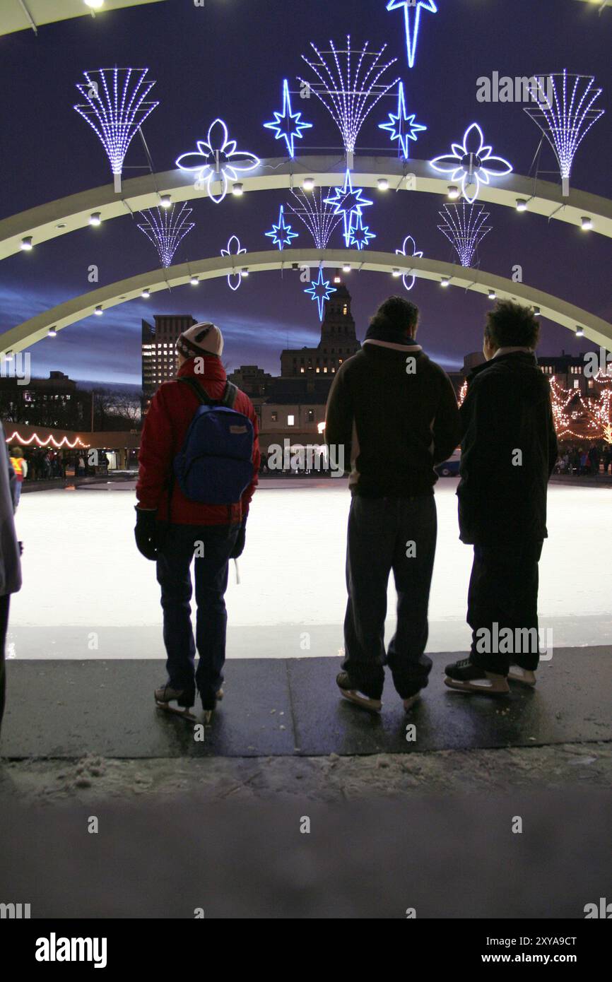 Winter scene: People ice skating under a festive light display ...