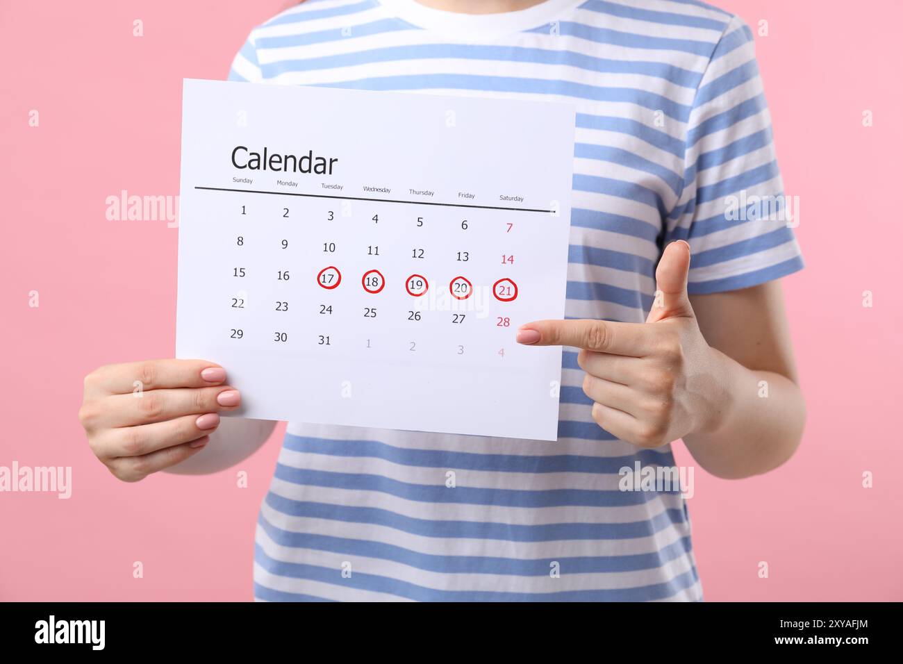 Woman holding calendar with marked menstrual cycle days on pink ...