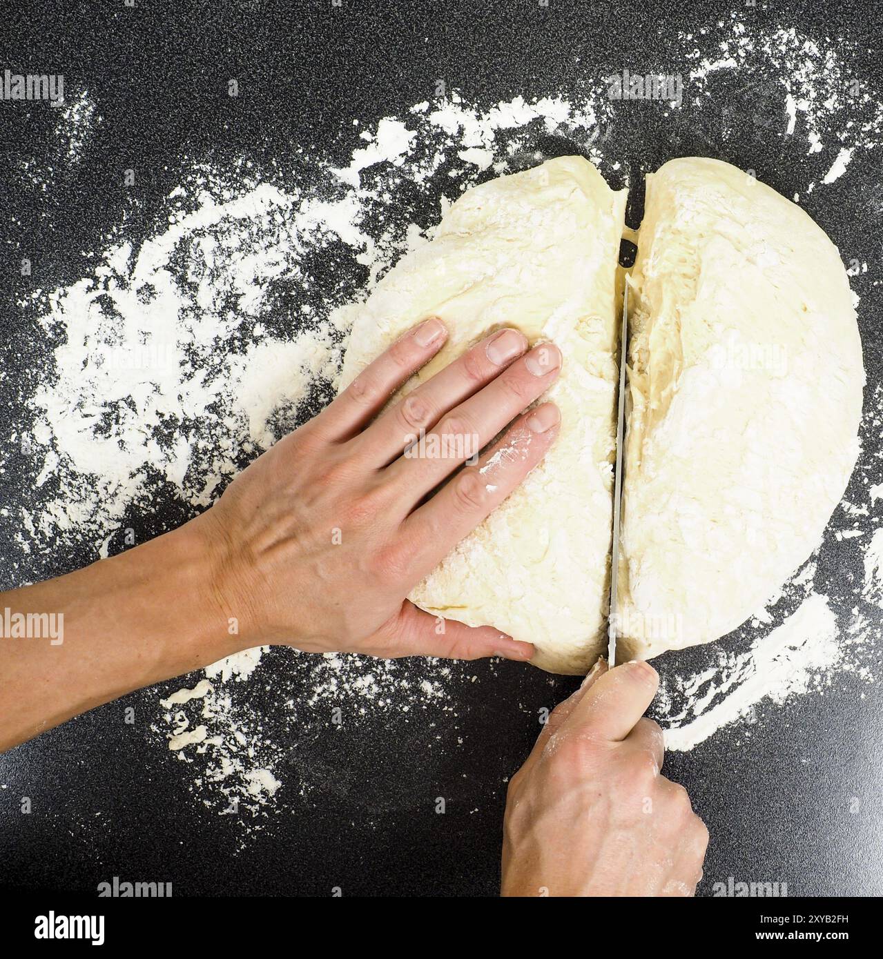 Hands cutting a lump of dough into two pieaces on black table with ...