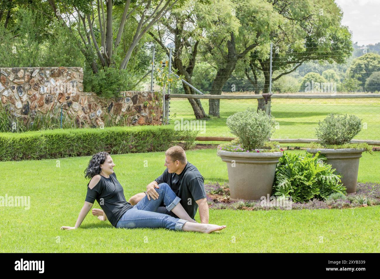 A young adult couple sitting outside their home on the lawn, talking to ...