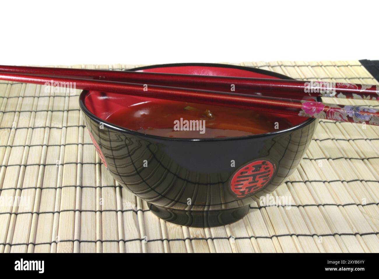 Thai soup with chopsticks on a raffia mat against a white background ...