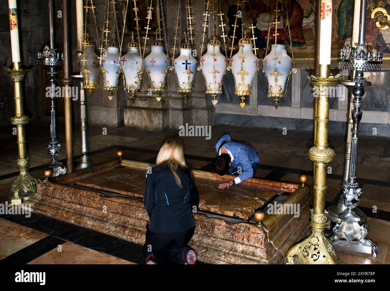 A woman kneeling and praying at the Stone of Anointing inside the ...