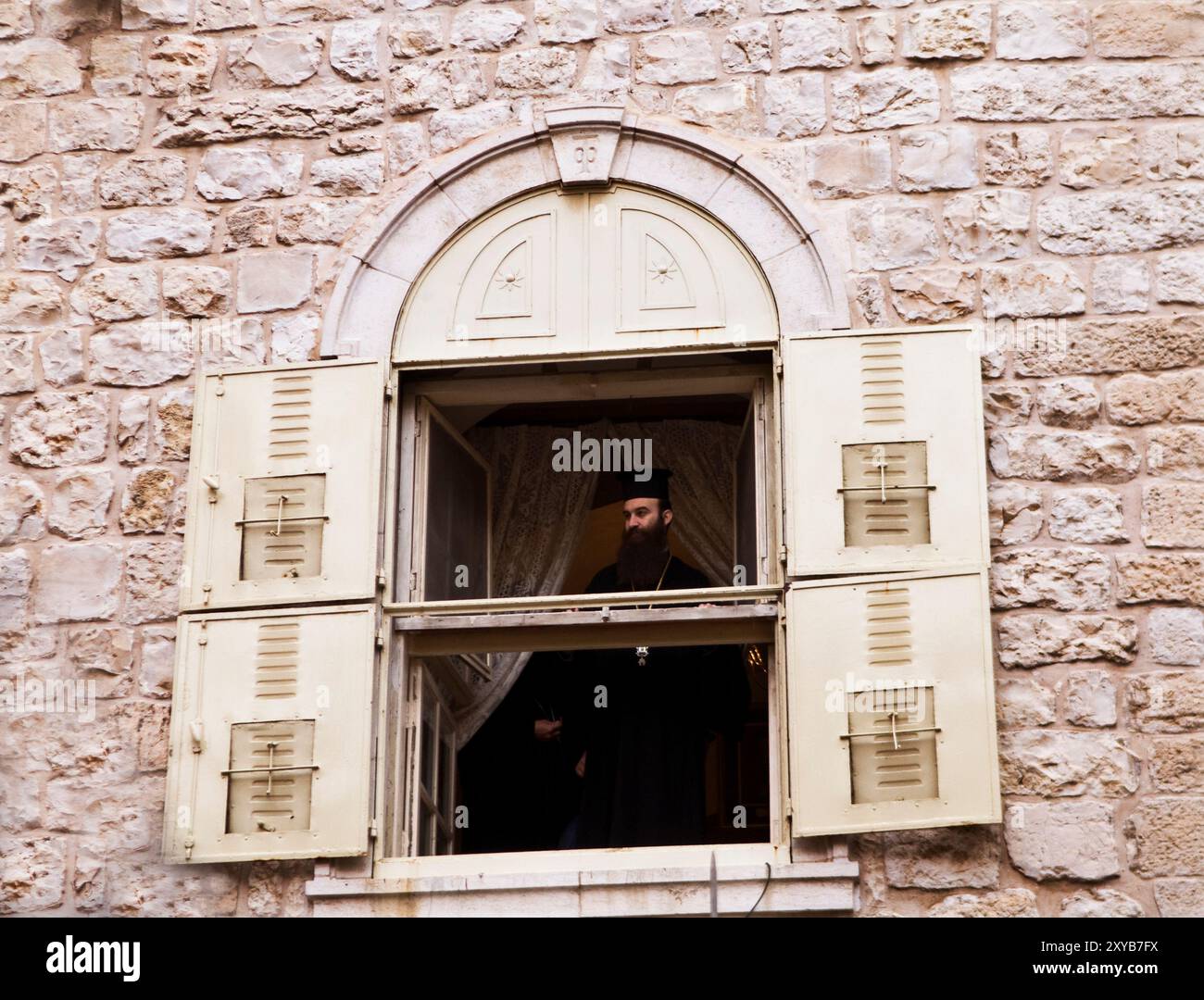 A Greek Orthodox priest looking out the window of the monastery by the ...